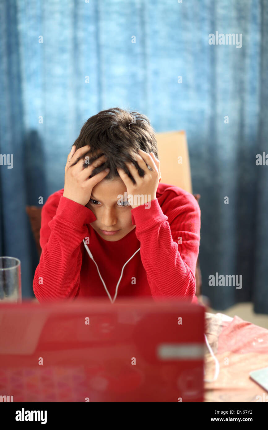 Young boy looks confused while doing his homework on a computer - with ...