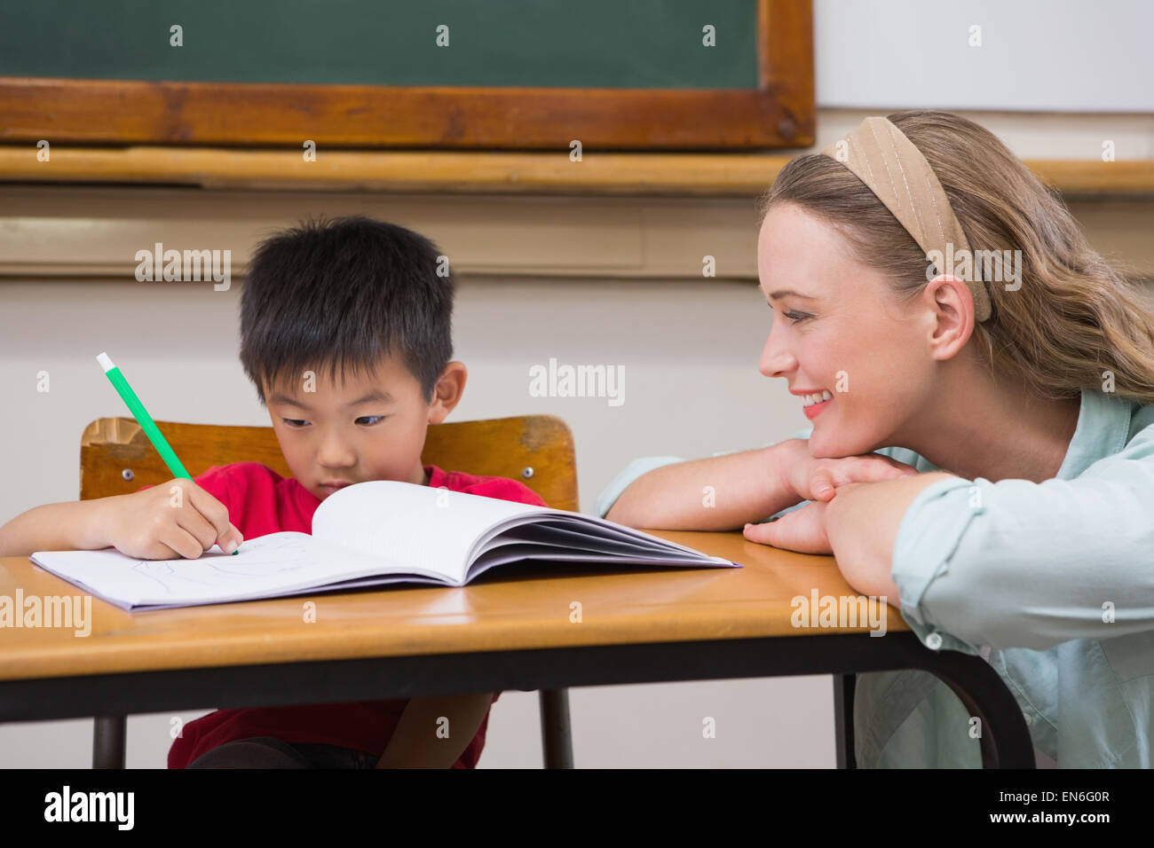 Teacher helping pupil in classroom Stock Photo - Alamy