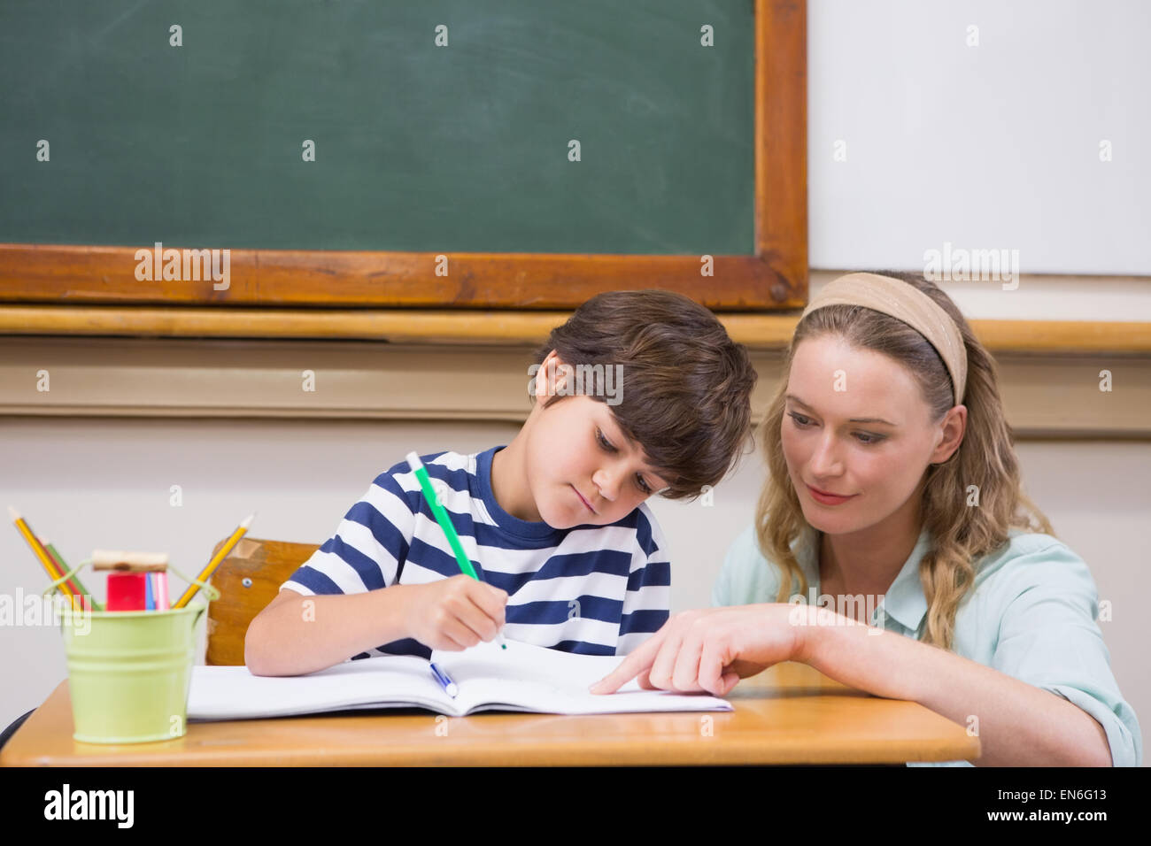 Teacher helping pupil in classroom Stock Photo - Alamy
