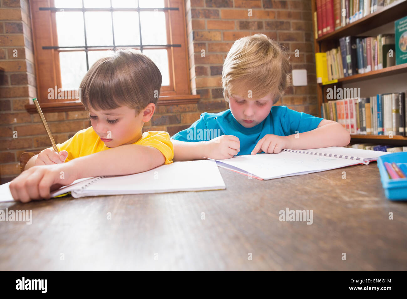 Cute pupils writing in library Stock Photo - Alamy