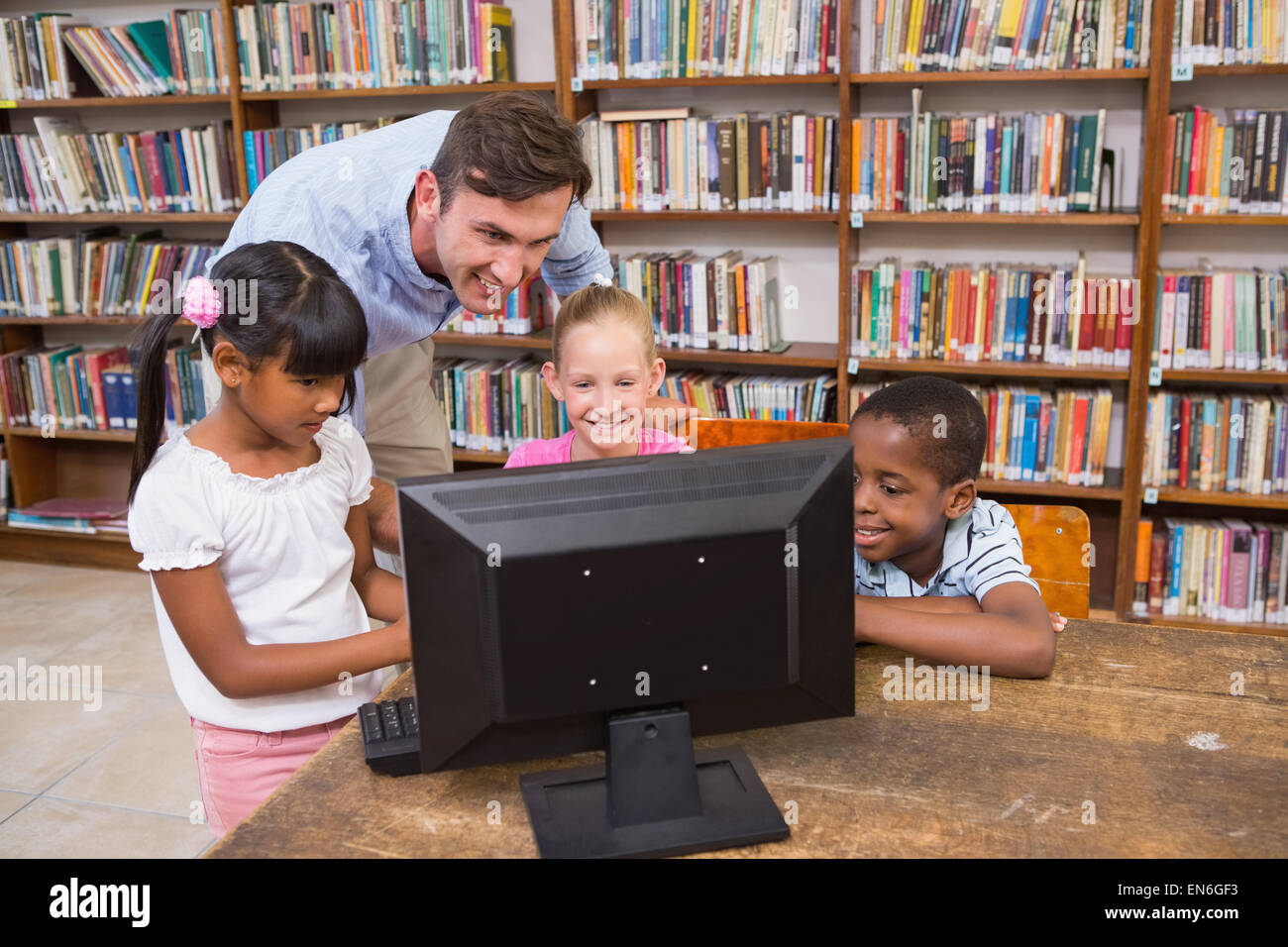 Teacher and pupils using computer at library Stock Photo - Alamy