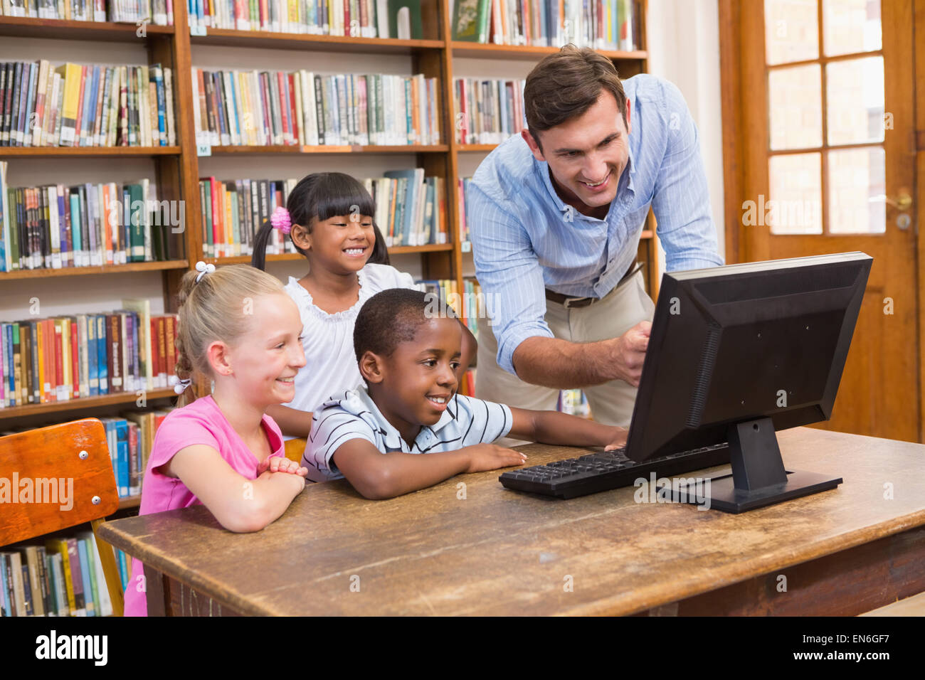Teacher and pupils using computer at library Stock Photo - Alamy