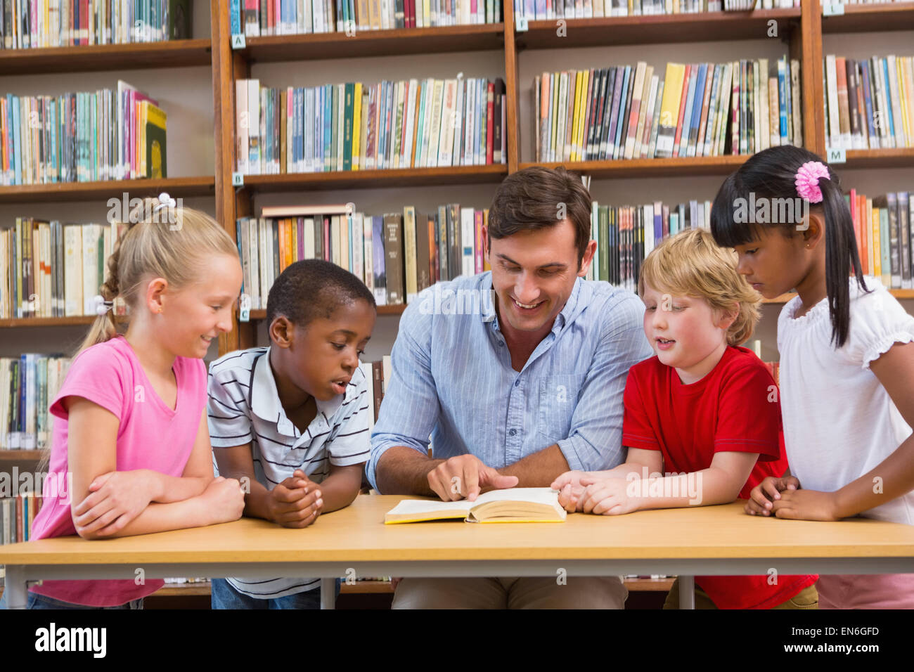 Teacher reading book to pupils at library Stock Photo - Alamy