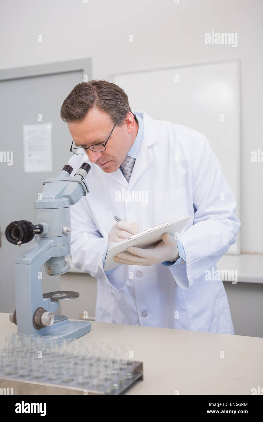 Scientist analysing microscope writing on clipboard Stock Photo - Alamy