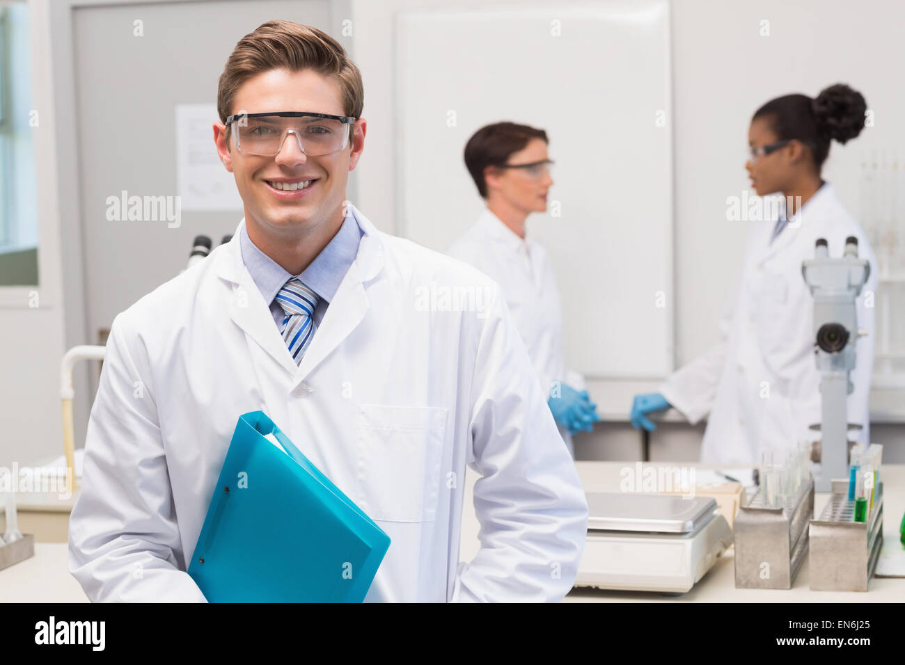 Scientist smiling at camera while colleagues talking together Stock ...