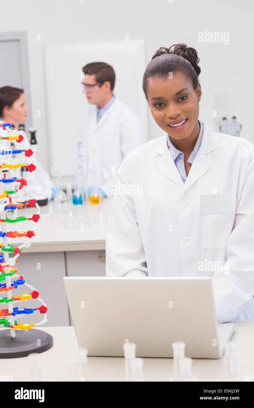 Smiling scientist using laptop while colleagues talking together Stock ...