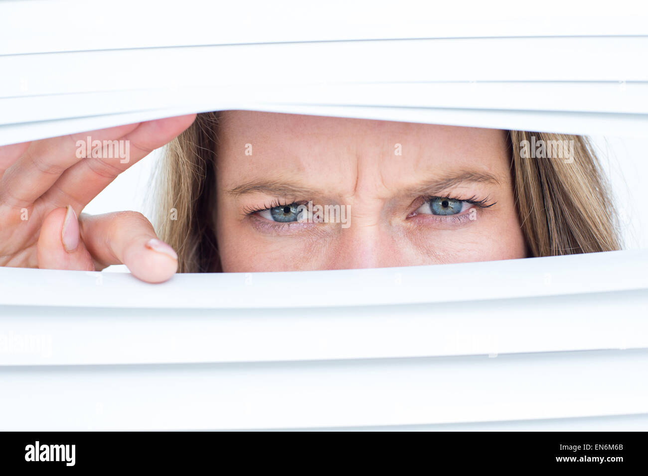 Woman peering through roller blind Stock Photo - Alamy