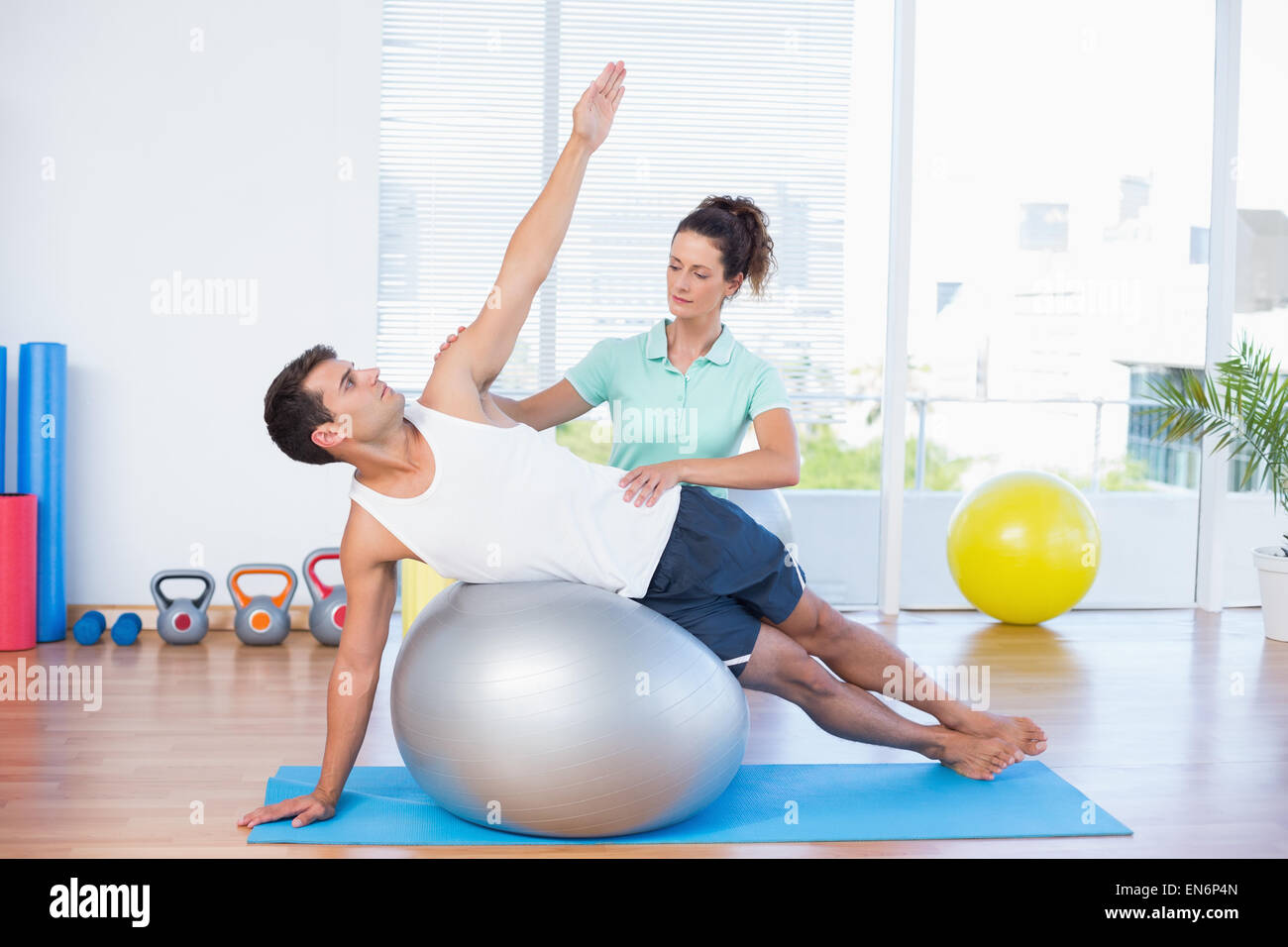 Trainer helping man with exercise ball Stock Photo - Alamy