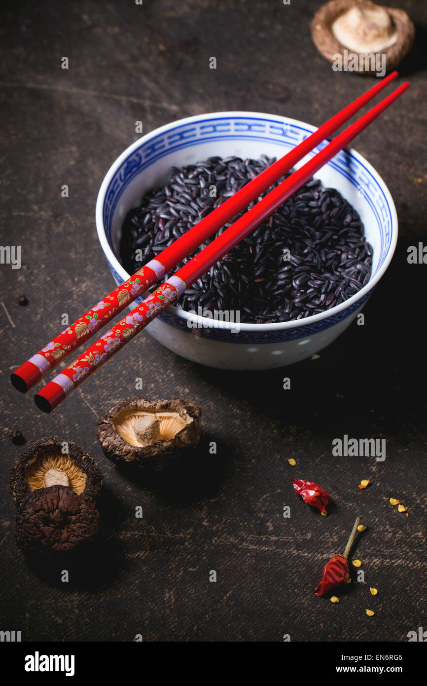 Porcelain bowl of uncooked black rice, served with dry shiitake ...