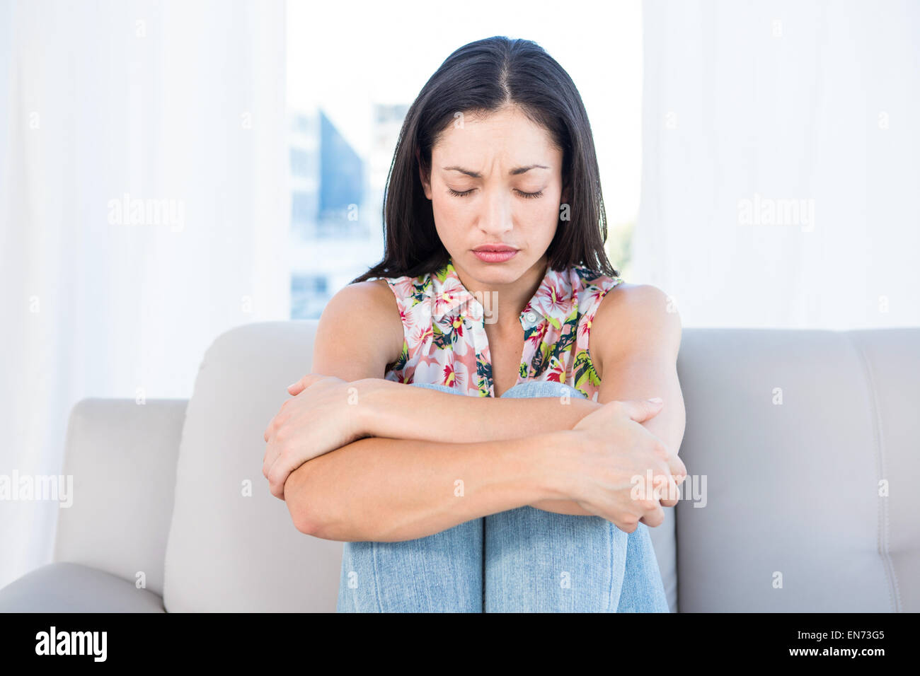 Pretty brunette feeling sad on couch Stock Photo - Alamy