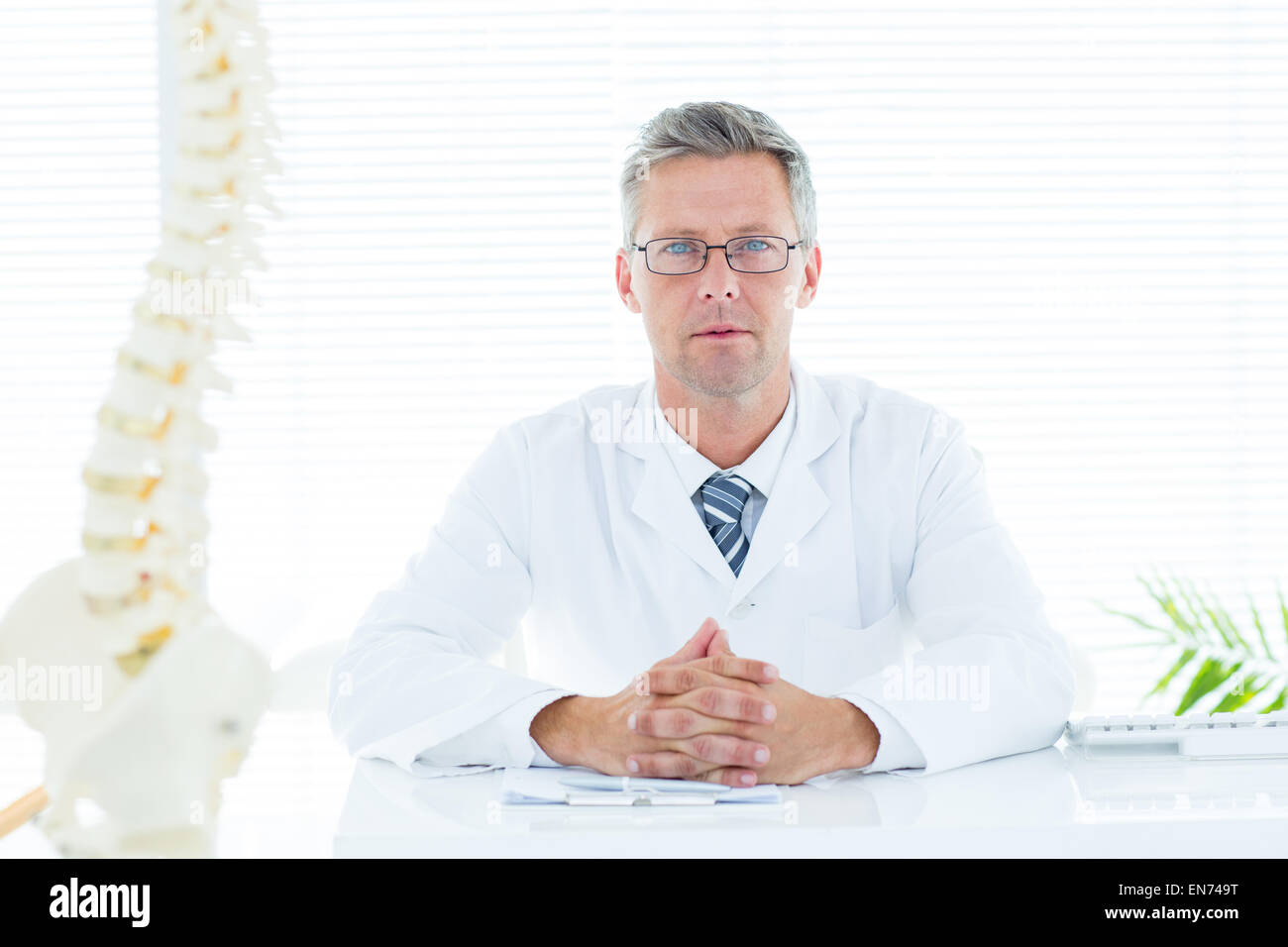 Doctor sitting at his desk looking at camera Stock Photo - Alamy