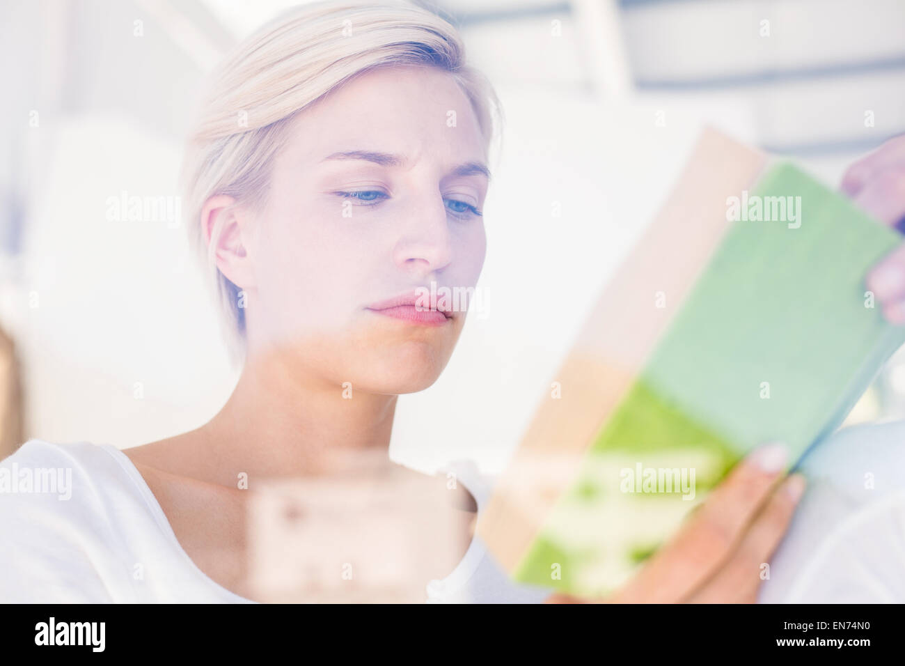 Thoughtful blonde woman reading a book Stock Photo - Alamy