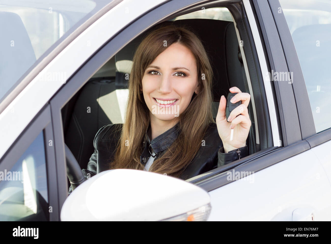 Young smiling woman in rental car with key in hand. Happy owner of the ...