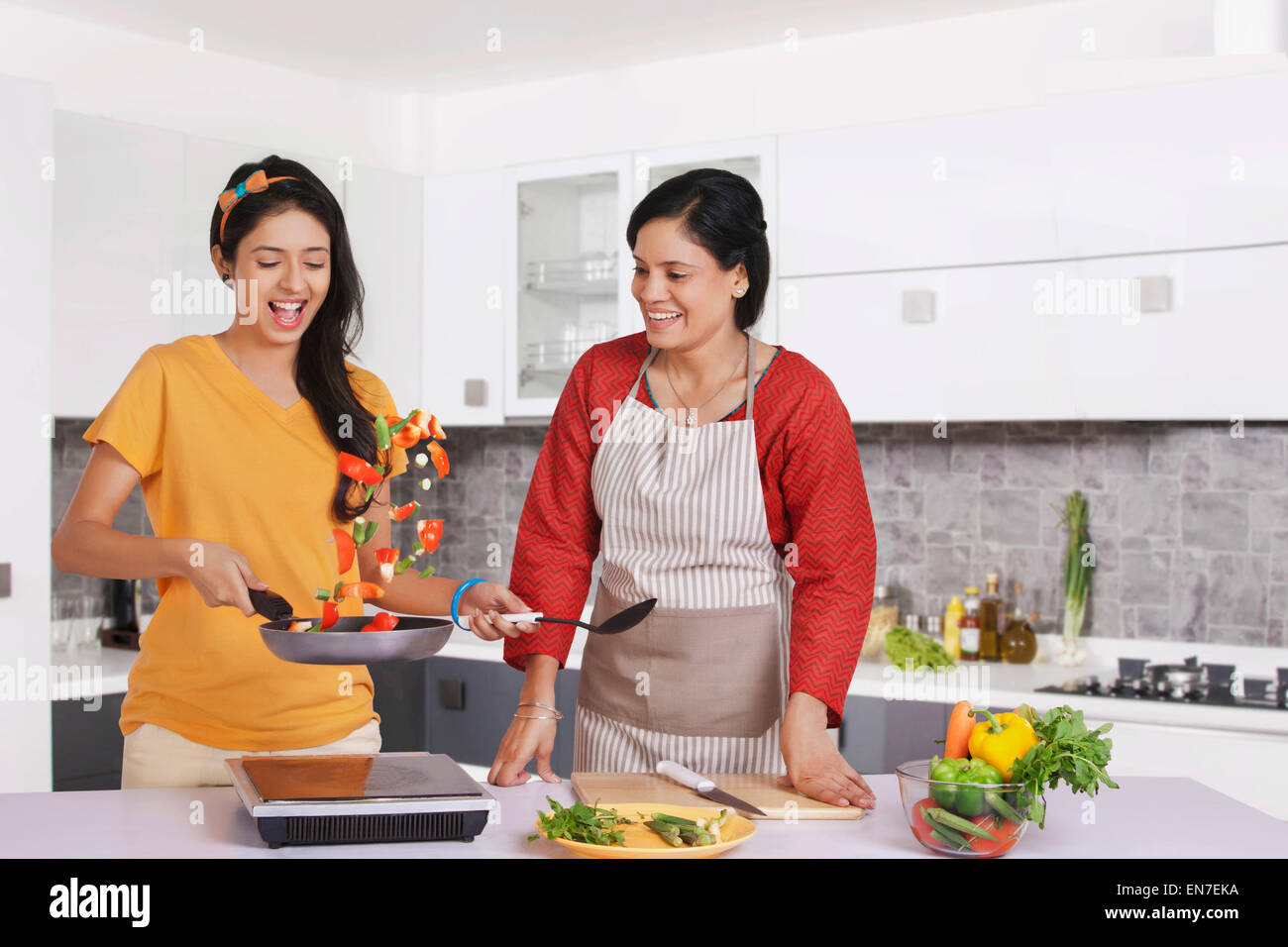 Girl cooking food while mother watches on Stock Photo - Alamy