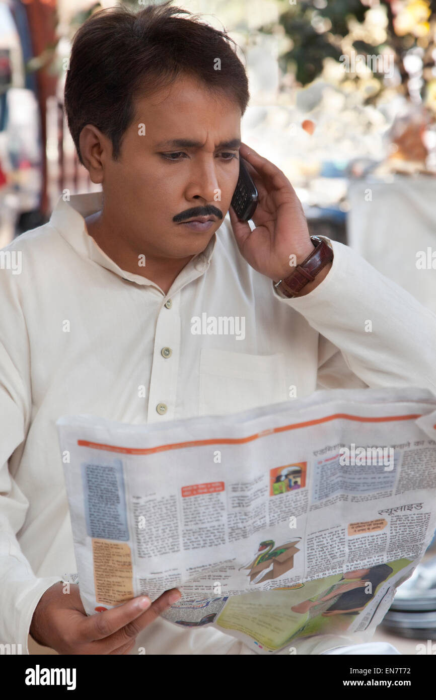 Man reading a newspaper and talking on a mobile phone Stock Photo - Alamy