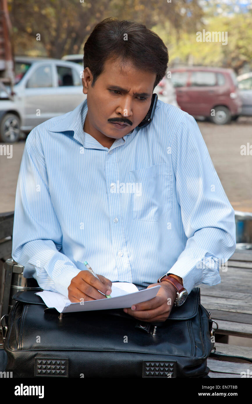 Salesman talking on a mobile phone and writing on paper Stock Photo - Alamy
