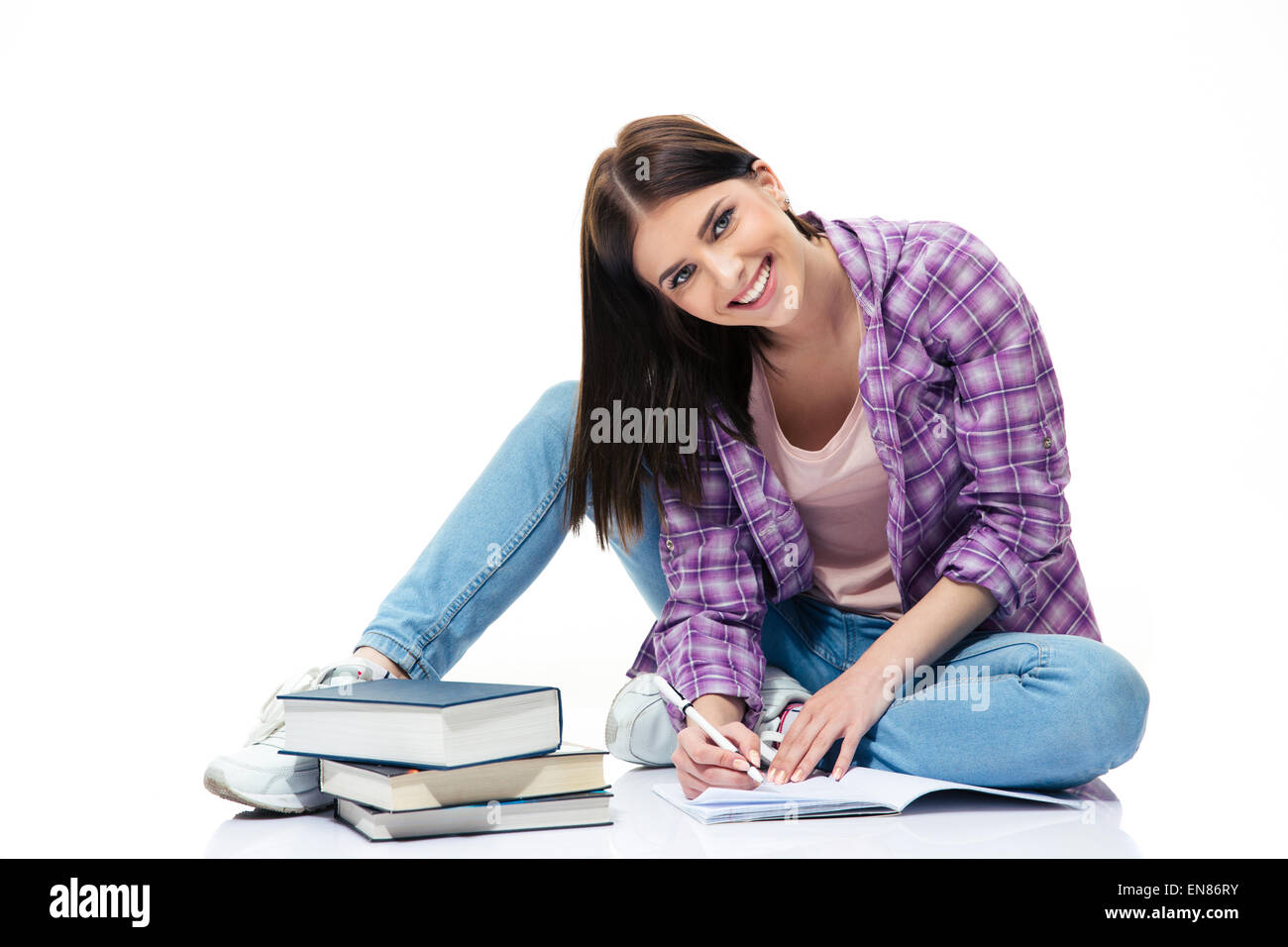 Happy woman sitting on the floor and writing in notebook over white ...