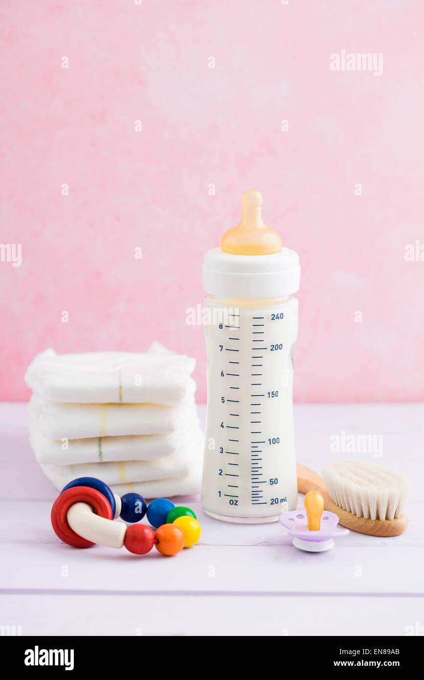 Baby bottle, pacifier, hairbrush, diapers and rattle on pink table ...