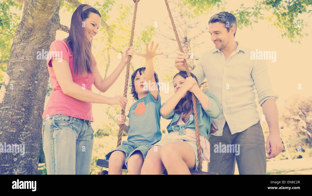 Happy couple pushing kids on swing Stock Photo - Alamy