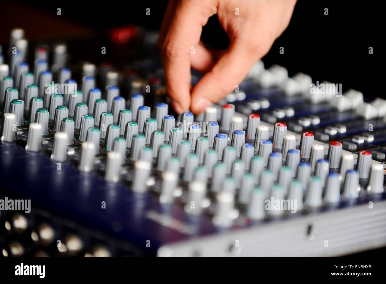Man's hand on a professional audio mixing console with adjusting knobs ...