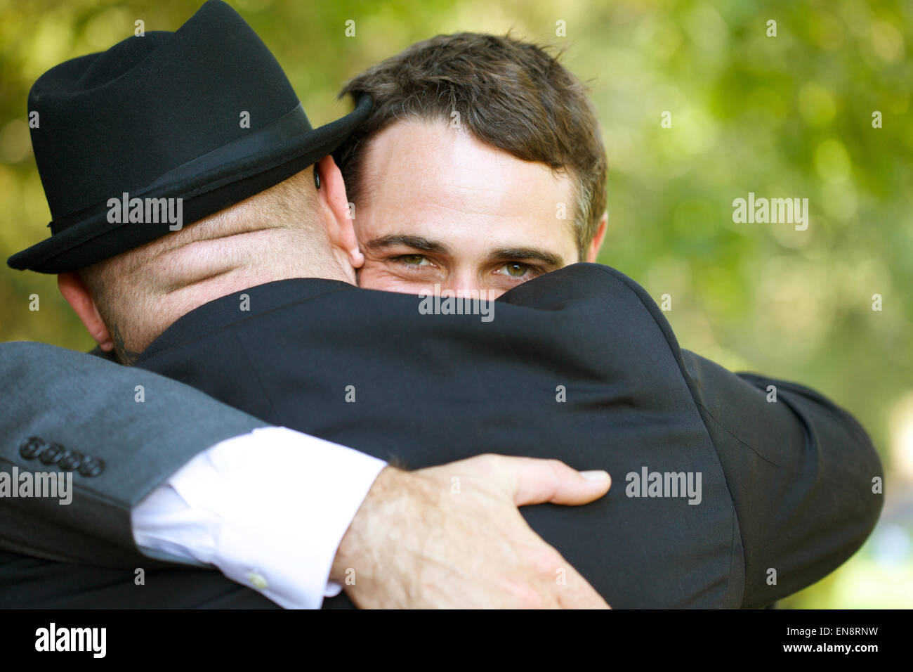 Two men embracing, the one facing the camera makes eye contact with the ...