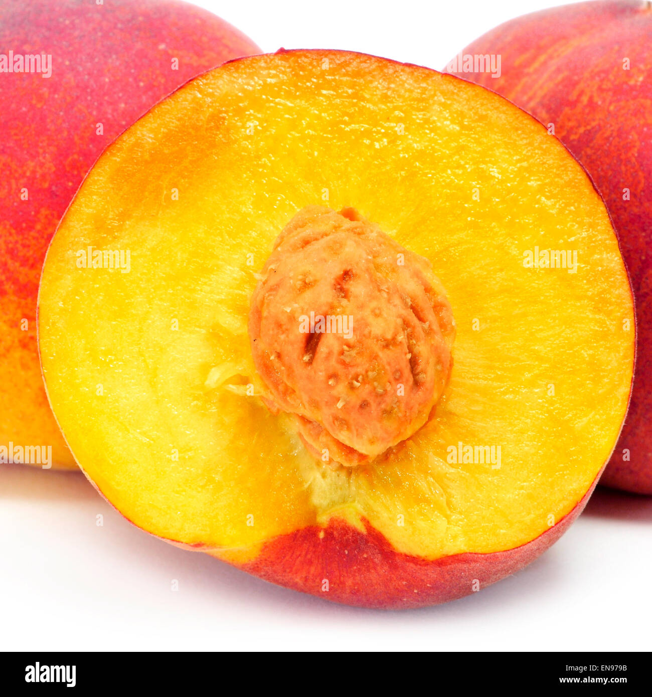 some peaches, one of them cut in halves showing its seed, on a white ...