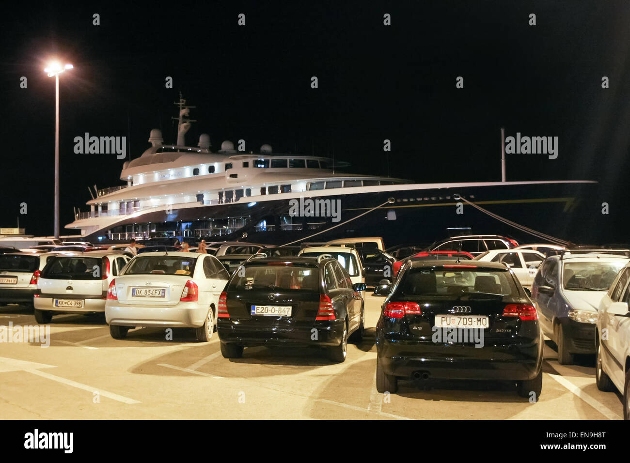 Cars parked on the dock in front of an anchored luxurious yacht ...