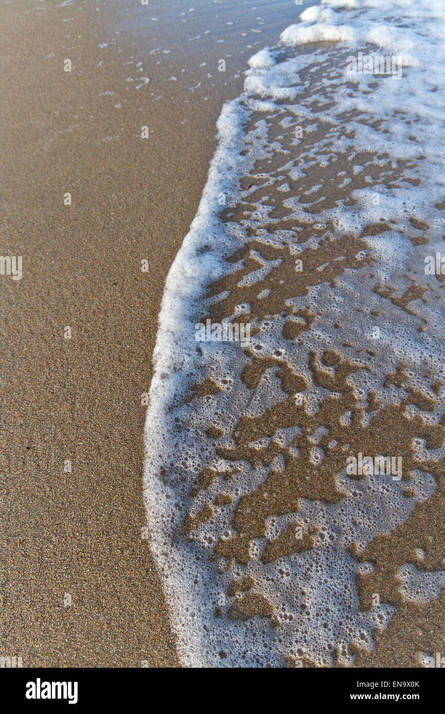 A foaming ocean tide coming up on a sandy beach shown as a vertical ...