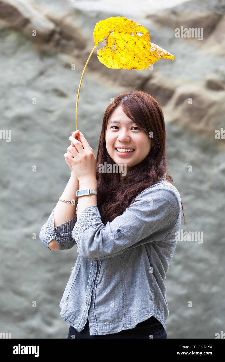 Young beautiful asian woman holding a yellow leaf up over her head like ...