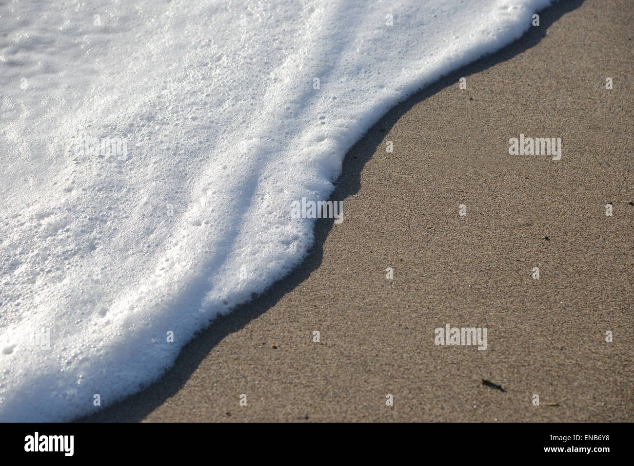 White surf bubbles up a sandy beach Stock Photo - Alamy