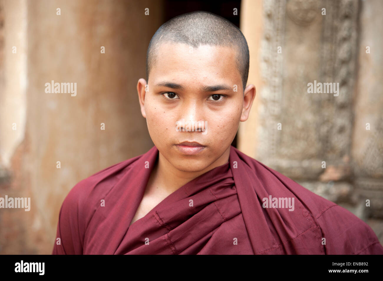 Portrait of a Buddhist monk wearing red robes against the stone wall ...