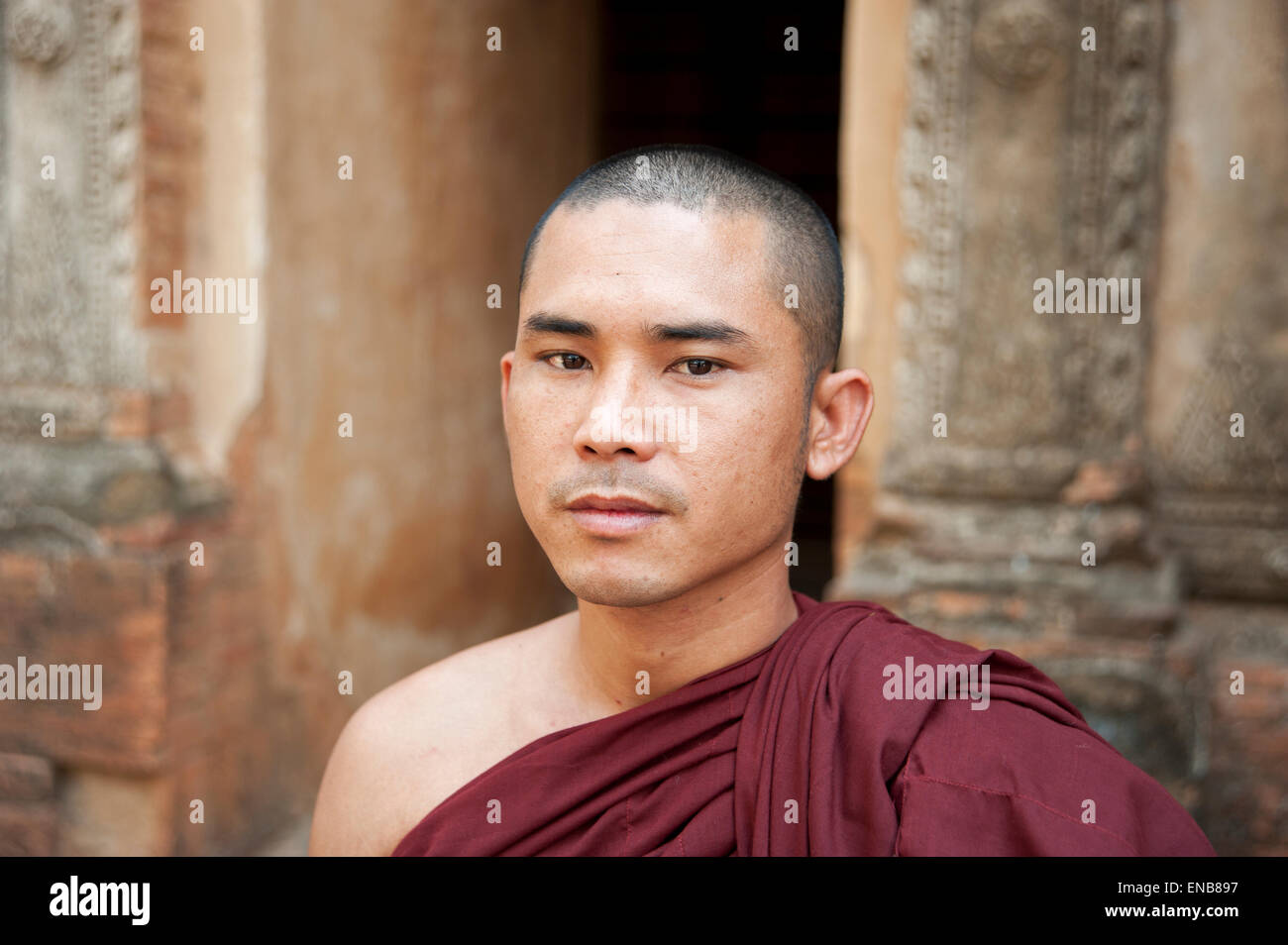 Portrait of a Buddhist monk wearing red robes against the stone wall ...