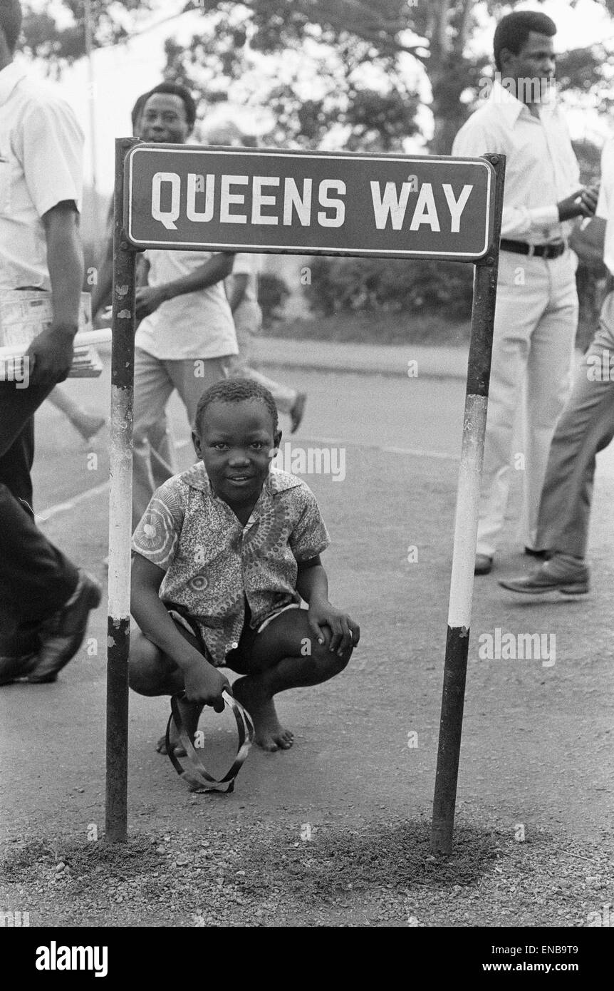 Young boy kneeling down bya road sign reading "Queens Way" in Kampala ...