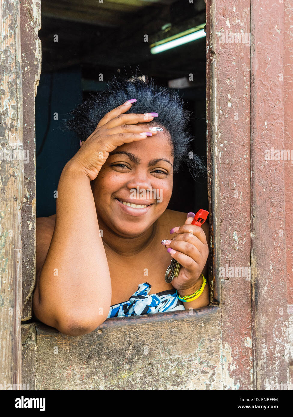 An Afro-Cuban woman leans on the ledge of a doorway opening and looks out toward the street in ...