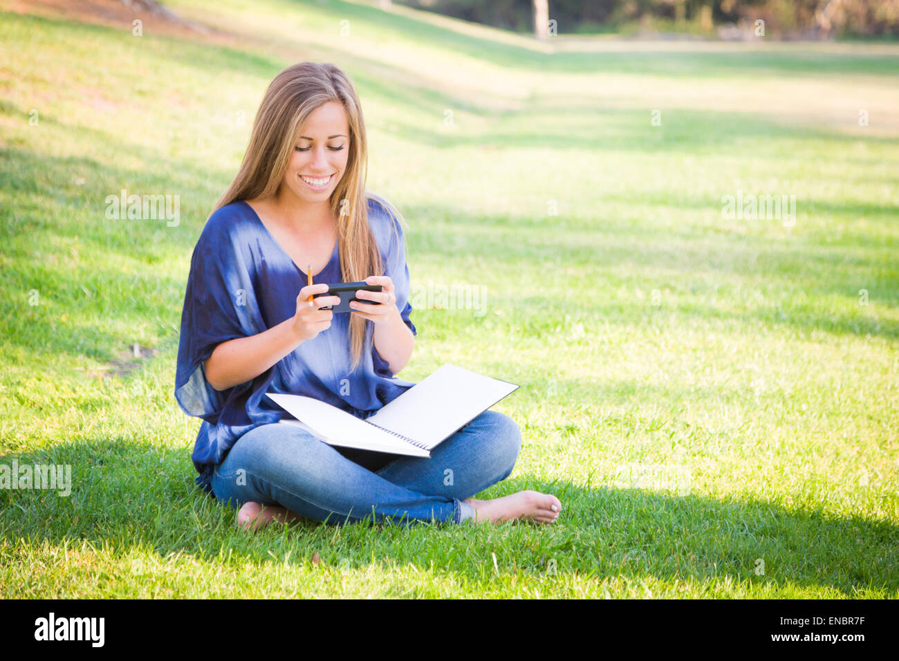Smiling Young Woman with Book and Cell Phone Outdoors at the Park Stock ...