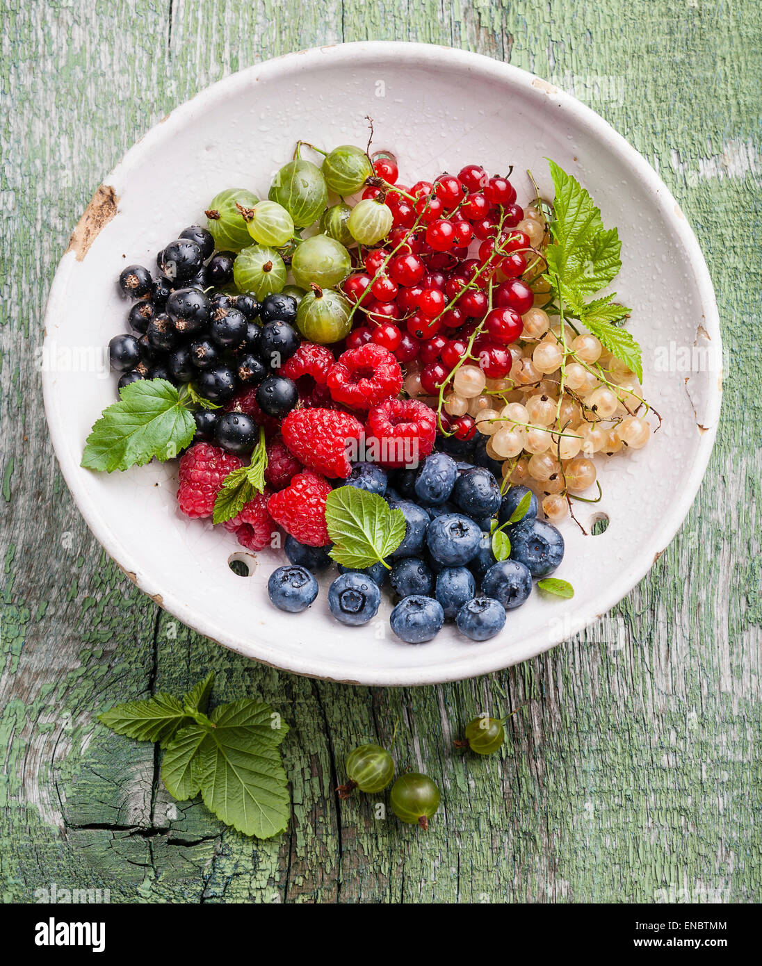 Mix of fresh berries with leaves in vintage ceramic colander on green ...