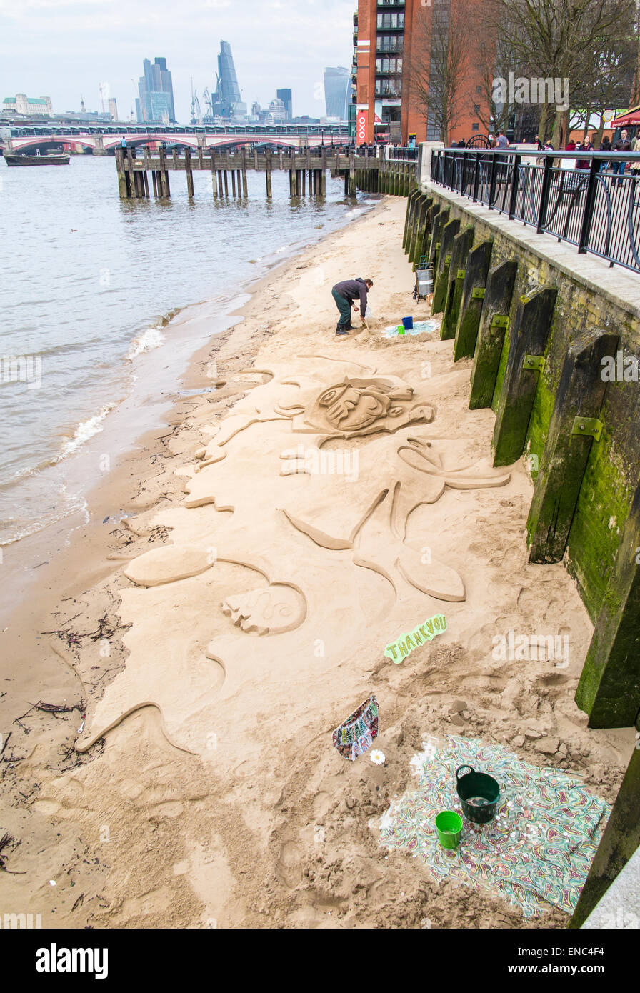 Sand sculptor making figures in the sand on a sand bank beside the ...