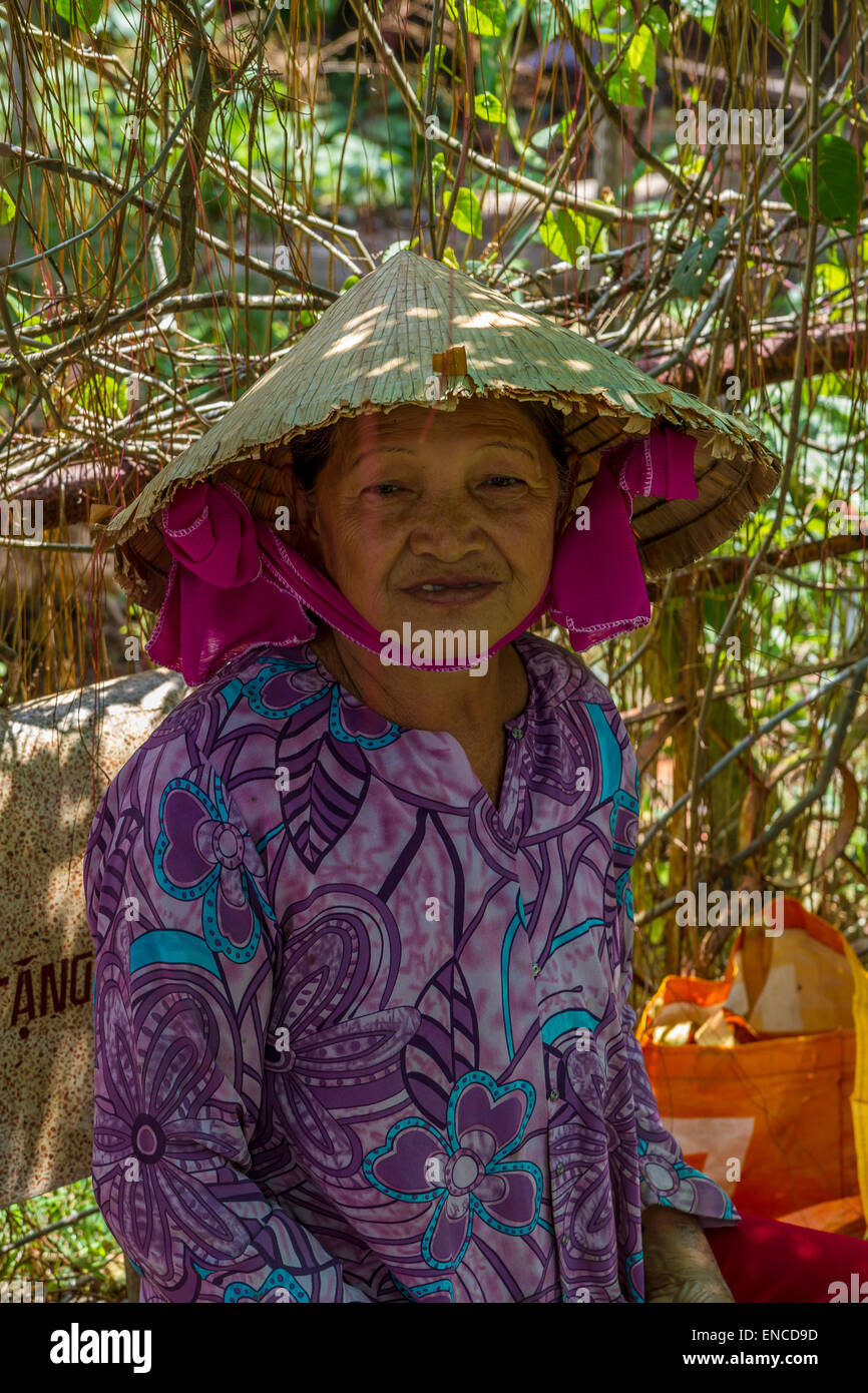 Elderly Vietnamese woman sits on a bench watching the passing tourists ...