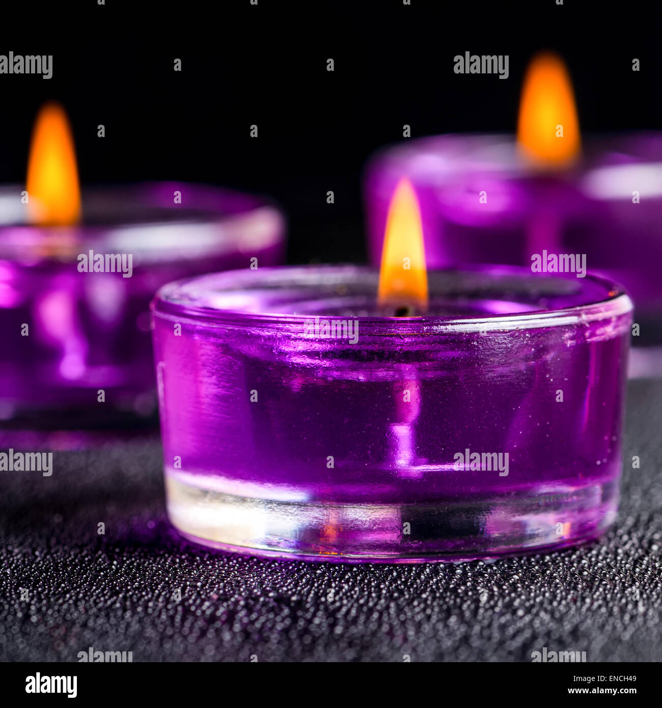 three beautiful purple candles on a black background with water drops ...