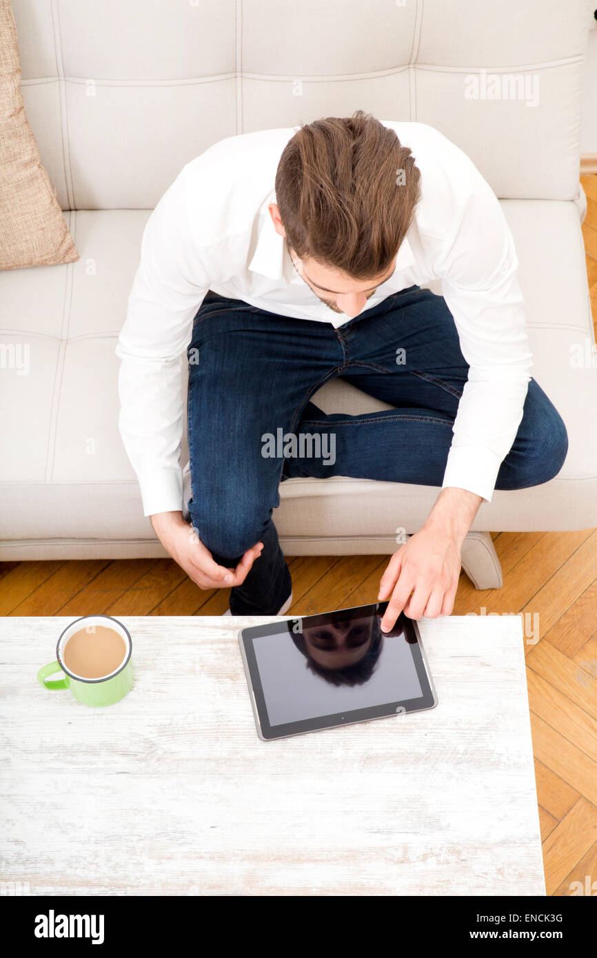 A young adult man sitting on the couch using a tablet Stock Photo - Alamy