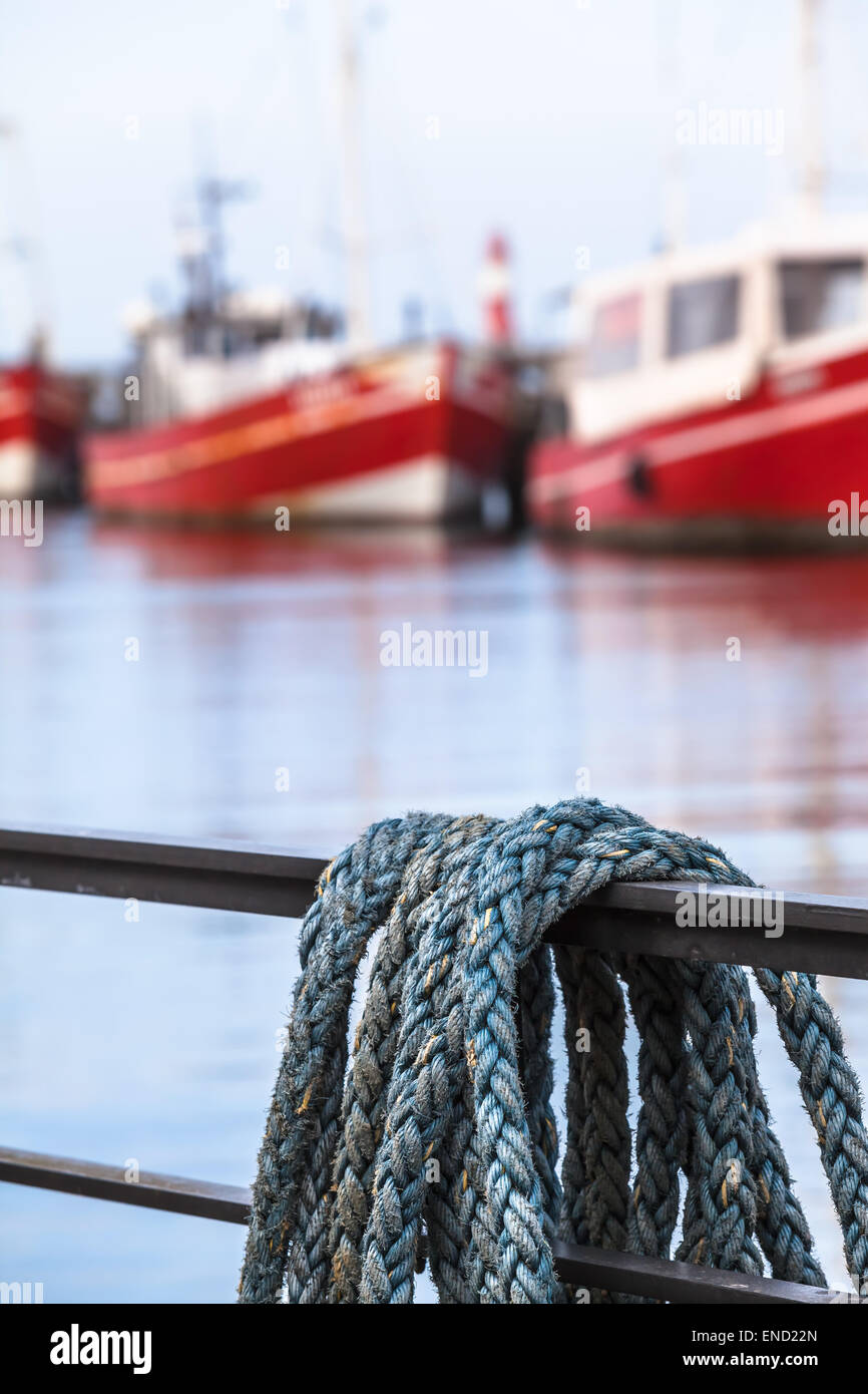 Thick rope hanging over a railing of the harbour and red fishing boats ...