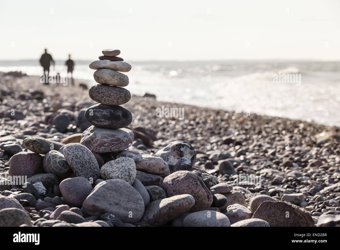 Stone stack at the beach and two people and a dog at the background ...
