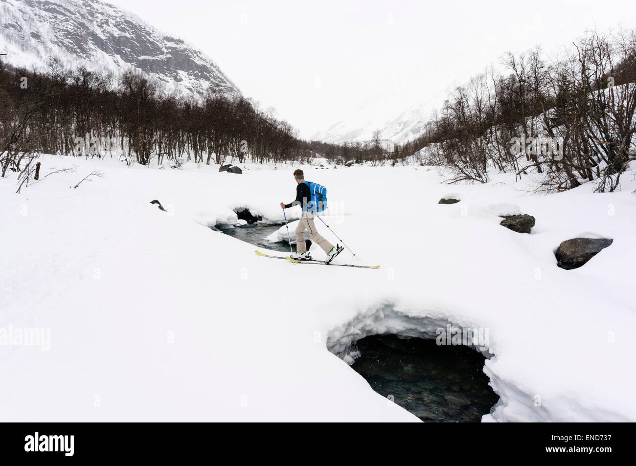 A skier ski touring along a river in snow on the way up Daltinden ...