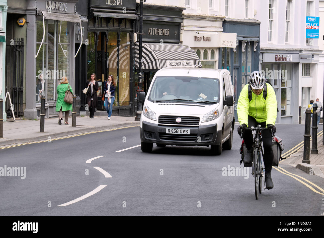 A van overtaking a cyclist wearing safety clothing on a shopping street ...