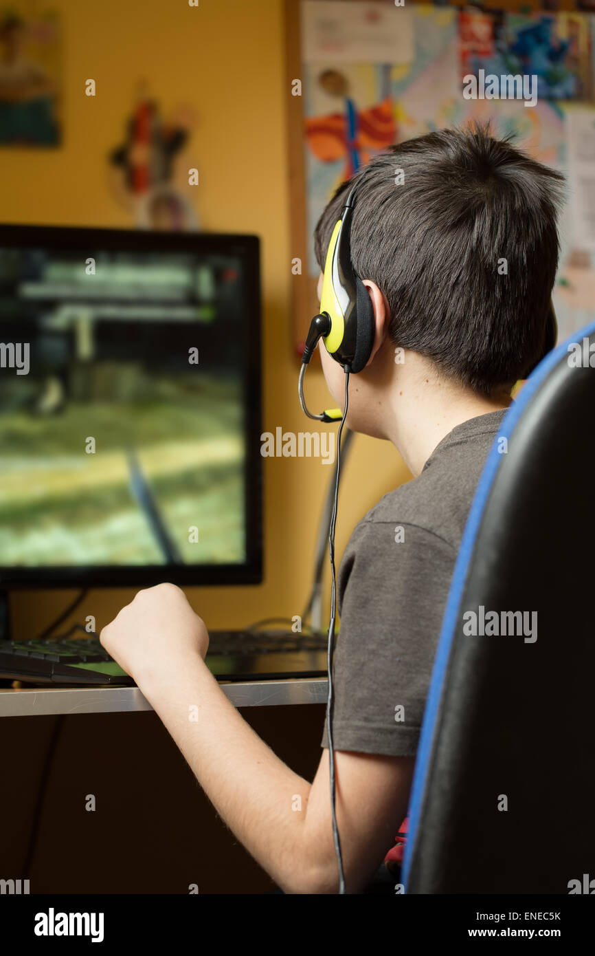 Teenager using computer at home with headphones, play game in his child ...