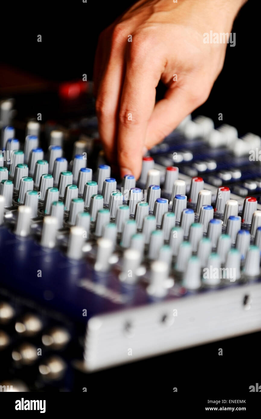 Man's hand on a professional audio mixing console with adjusting knobs ...