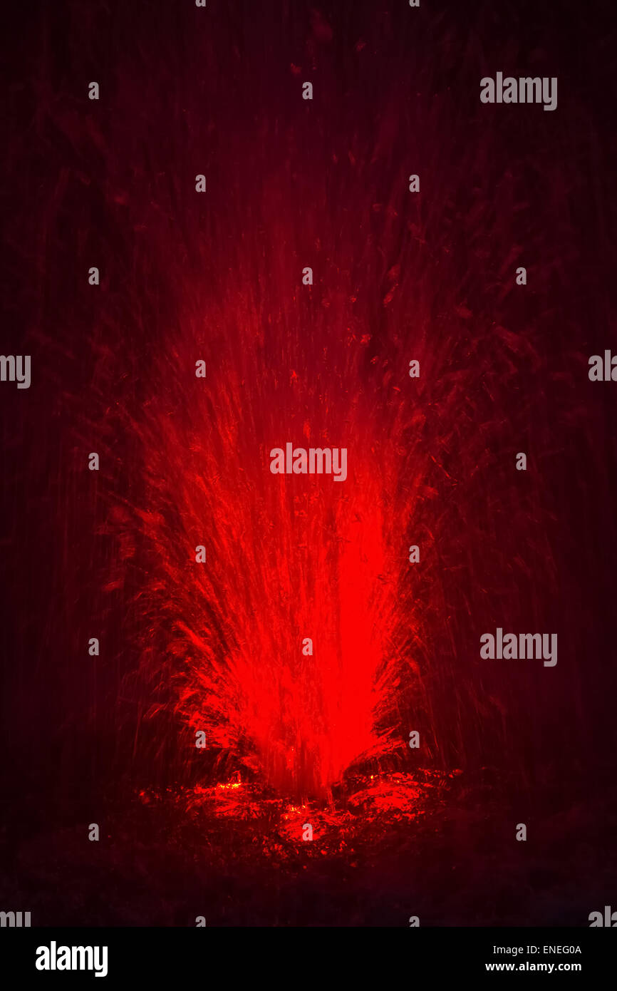Colorful fountain splashes red color of water drops on a black ...