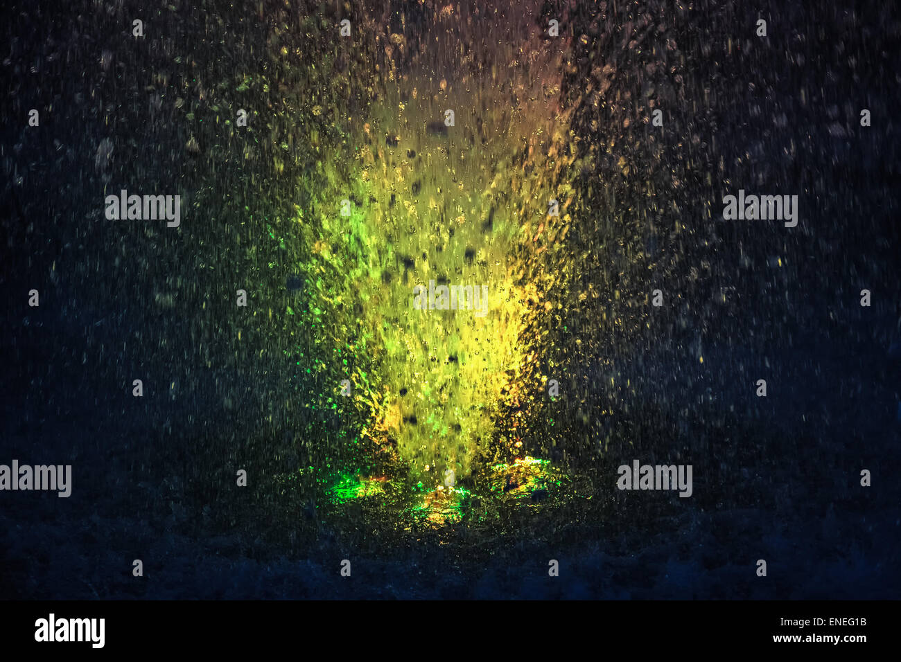 Colorful fountain splashes light yellow color of water drops on a black ...