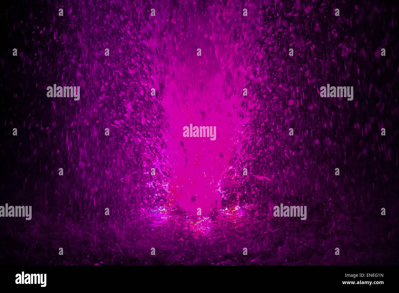 Colorful fountain splashes pink color of water drops on a black ...