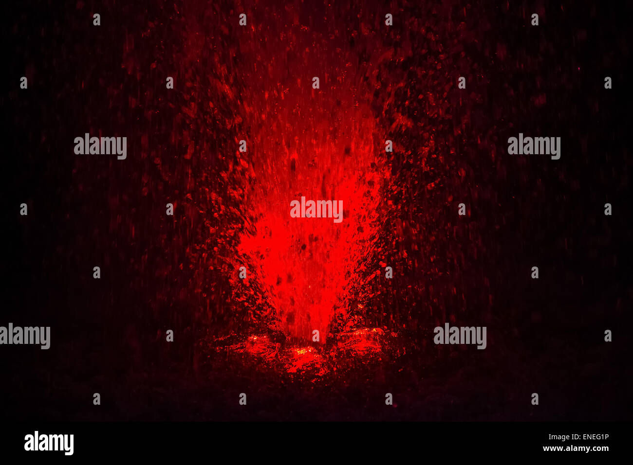 Colorful fountain splashes red color of water drops on a black ...